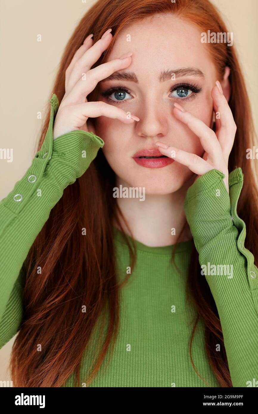 Young ginger female with clean skin touching face and looking at camera ...