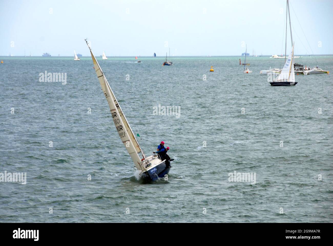 Small yacht heeling in a stiff breeze and crew of two sitting on the ...