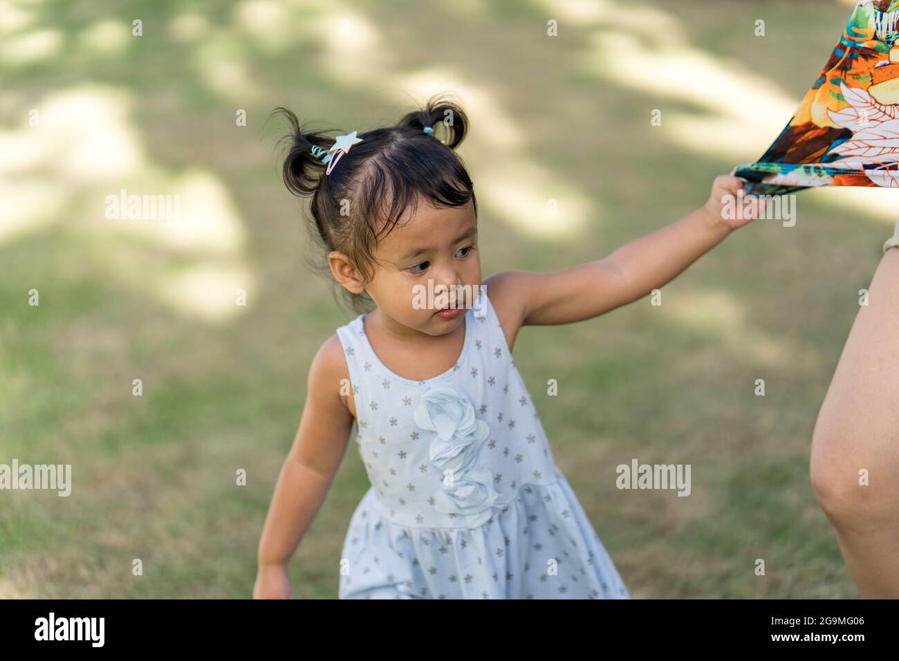 Cute Asian female child pulling on her mother's dress Stock Photo - Alamy