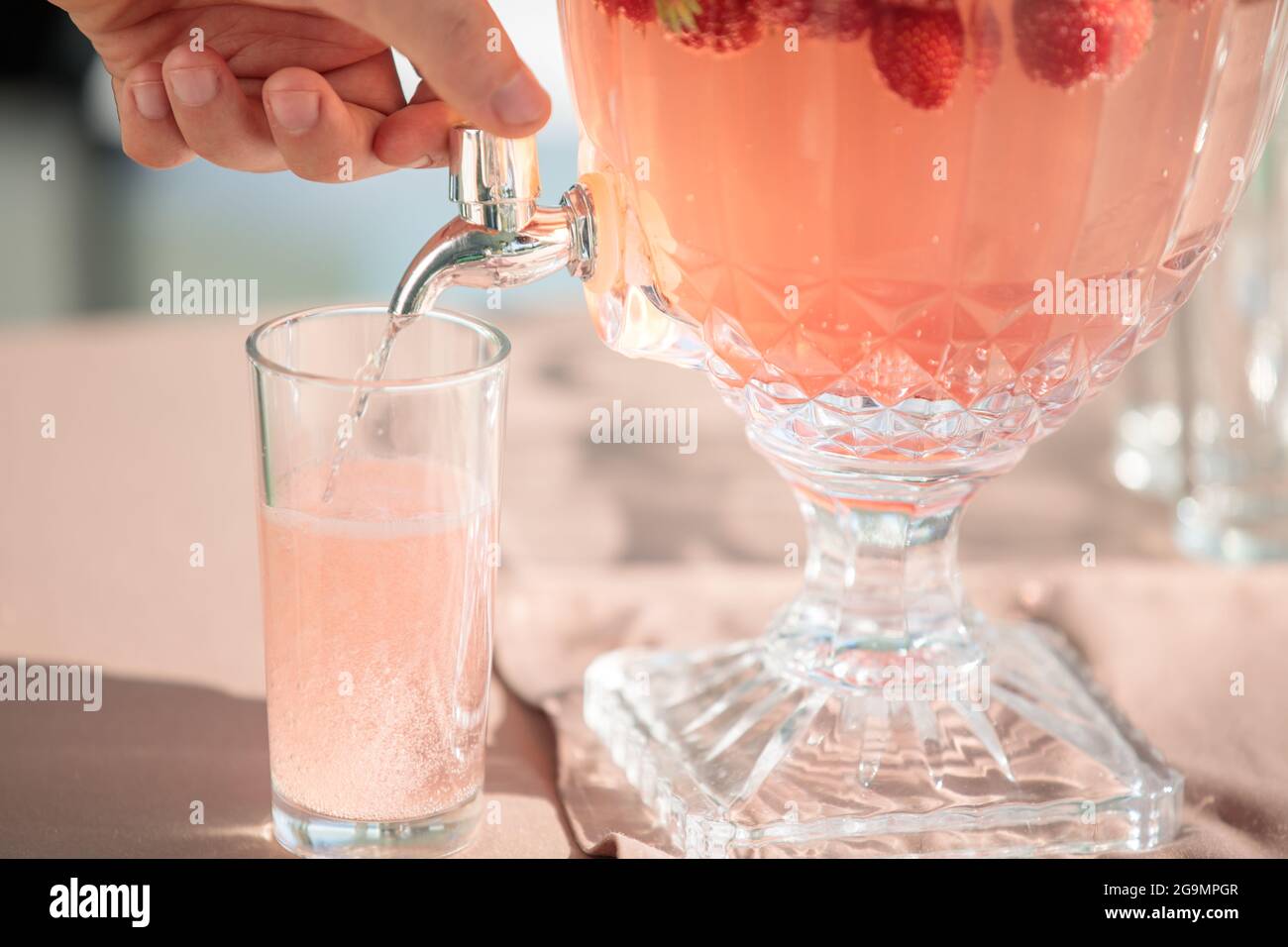 hand pouring lemonade from a can with a faucet, strawberries floats in ...