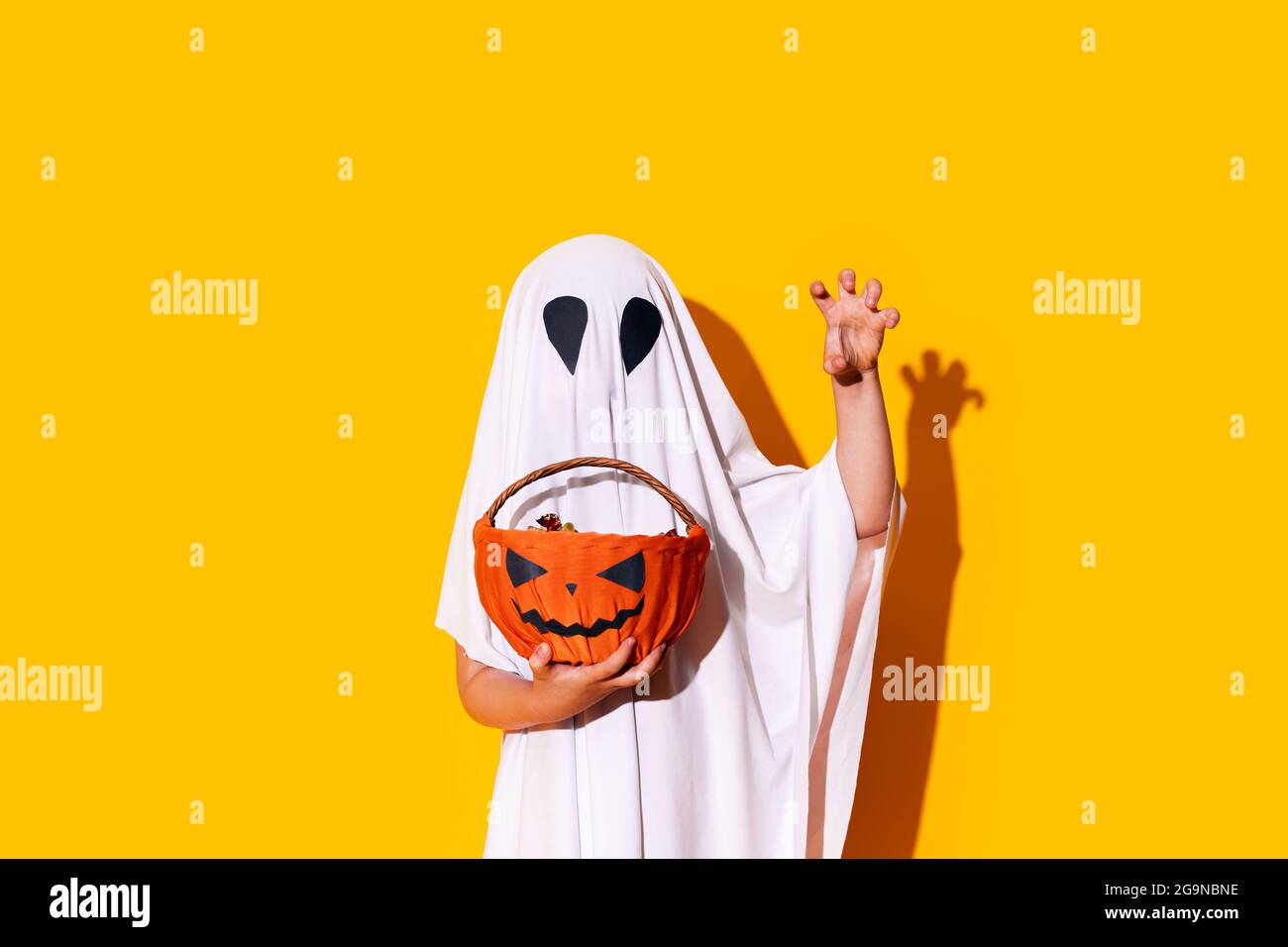 Child in ghost costume holding basket of chocolates in one hand, and ...