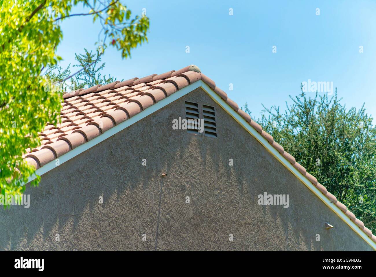 Tiled roof of a house and green-leafed trees under a clear blue sky ...