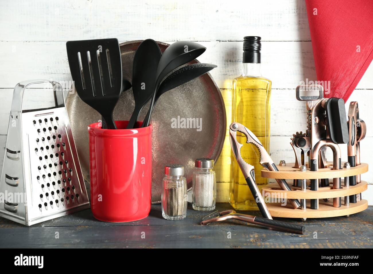 Plastic kitchen utensils in red cup with bottle of olive oil on wooden ...