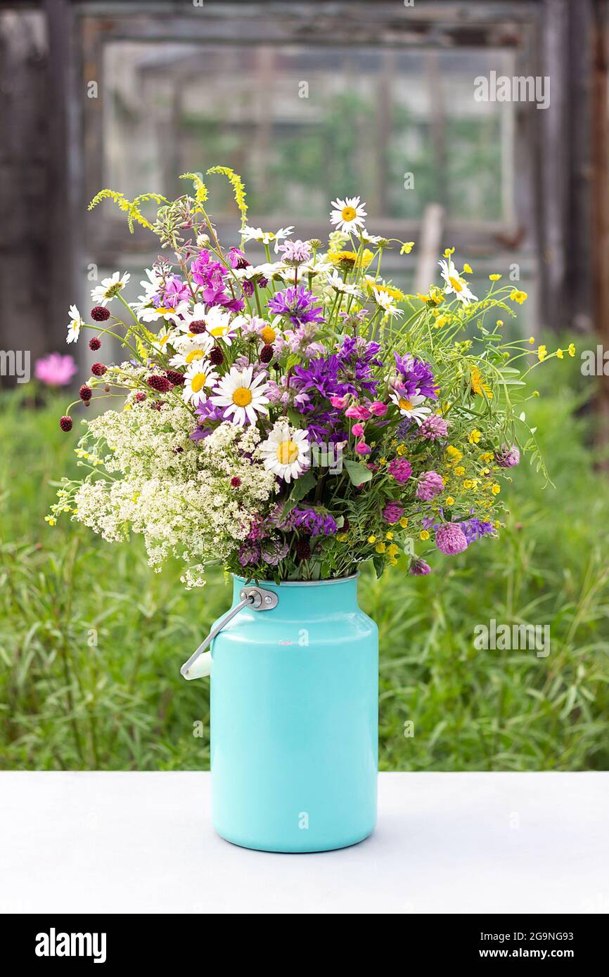 Bouquet of bright wild flowers in tin can vase on table outdoors, rural ...