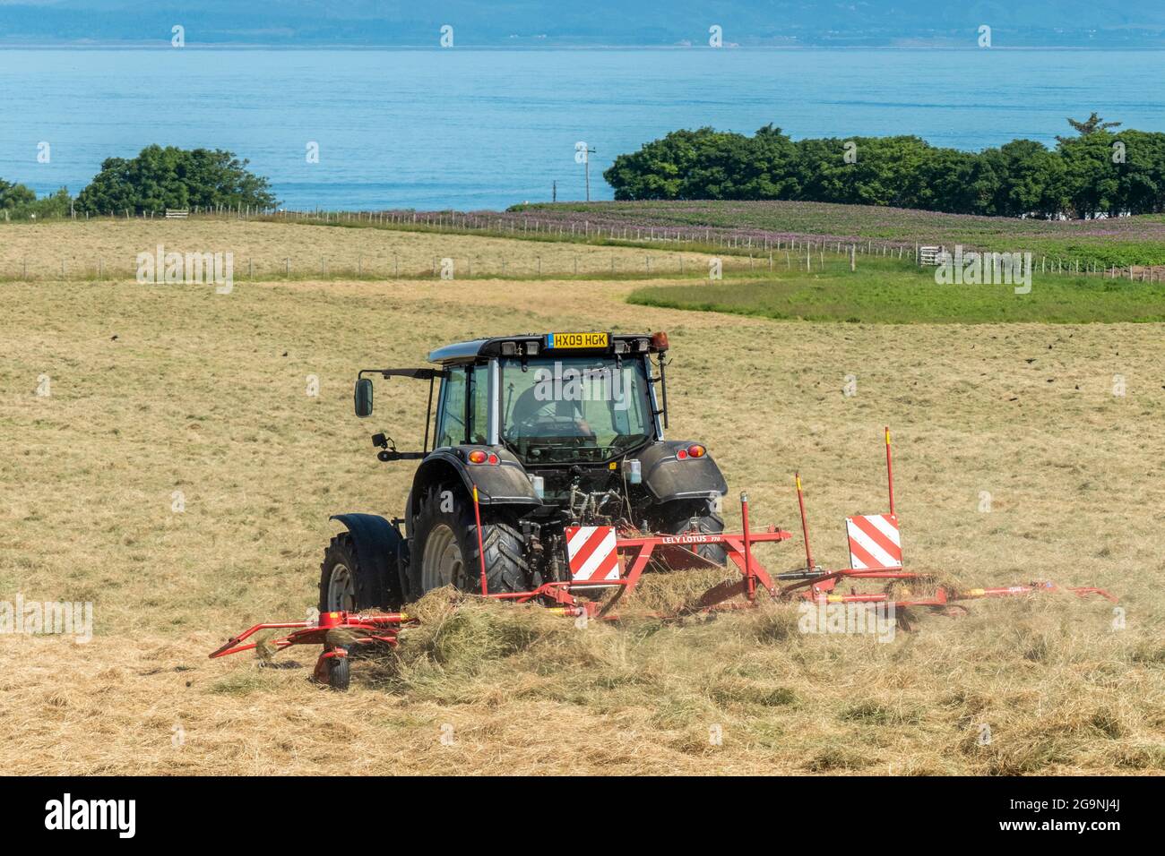Tractor and haybob machine turning hay near Portmahomack, Easter Ross ...