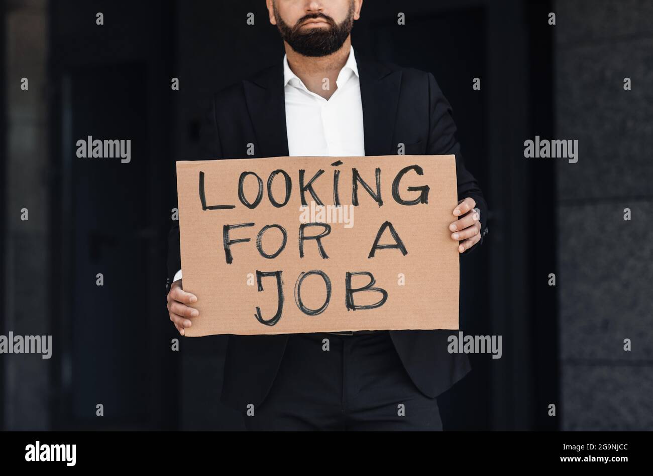 Male office worker in suit holding cardboard sign written looking for a ...