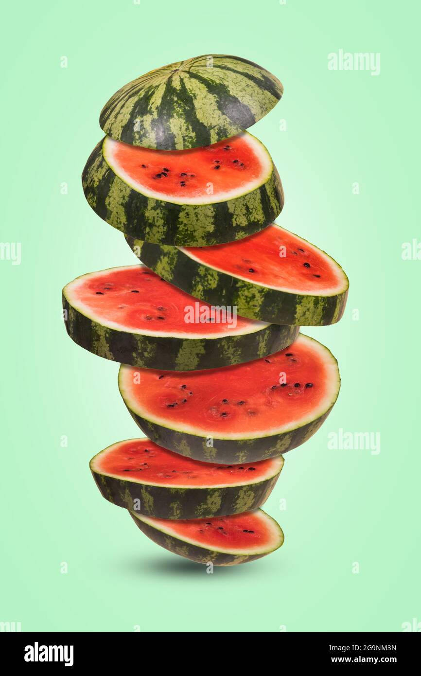 Ripe watermelon cut into pieces flying in the air on a light green ...