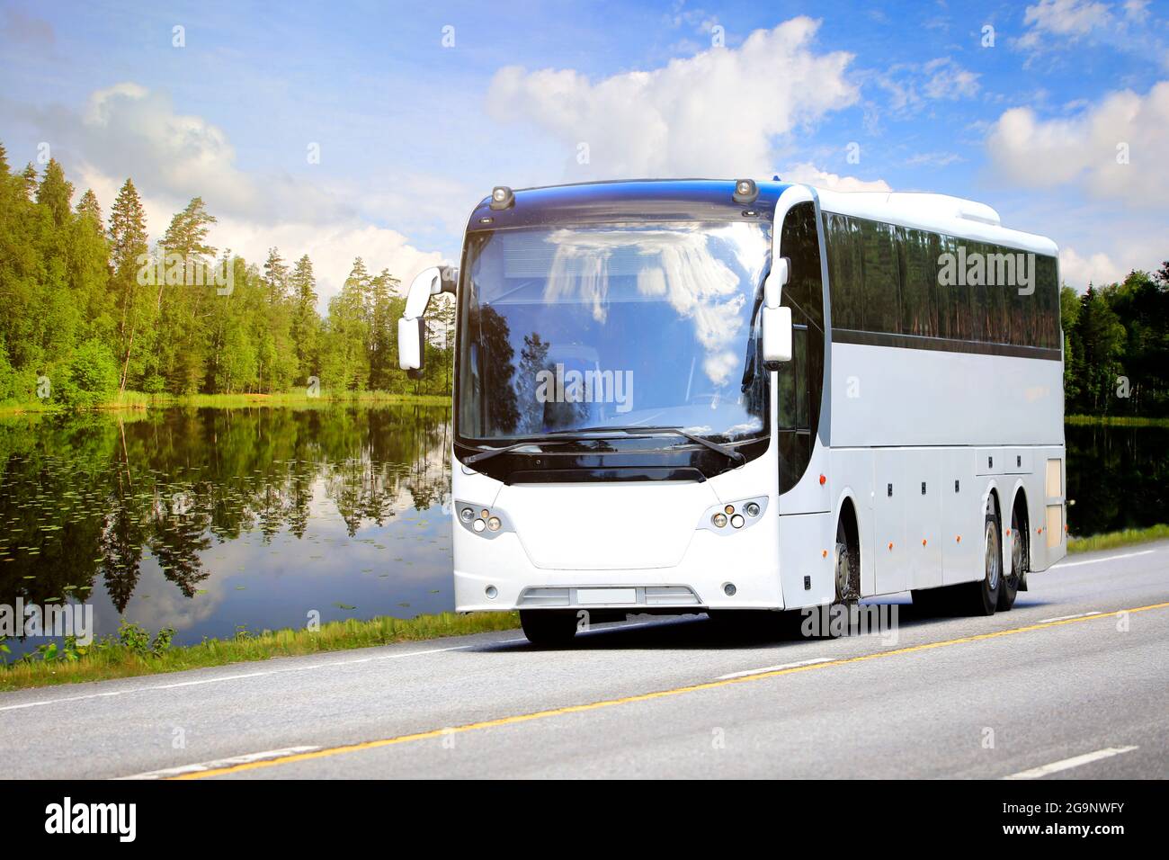 White coach bus travels on highway through rural scenery of a calm lake ...