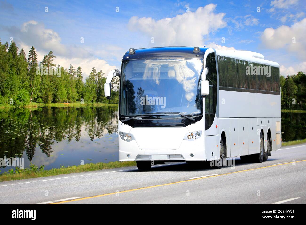 White coach bus travels on highway through rural scenery of a calm lake ...