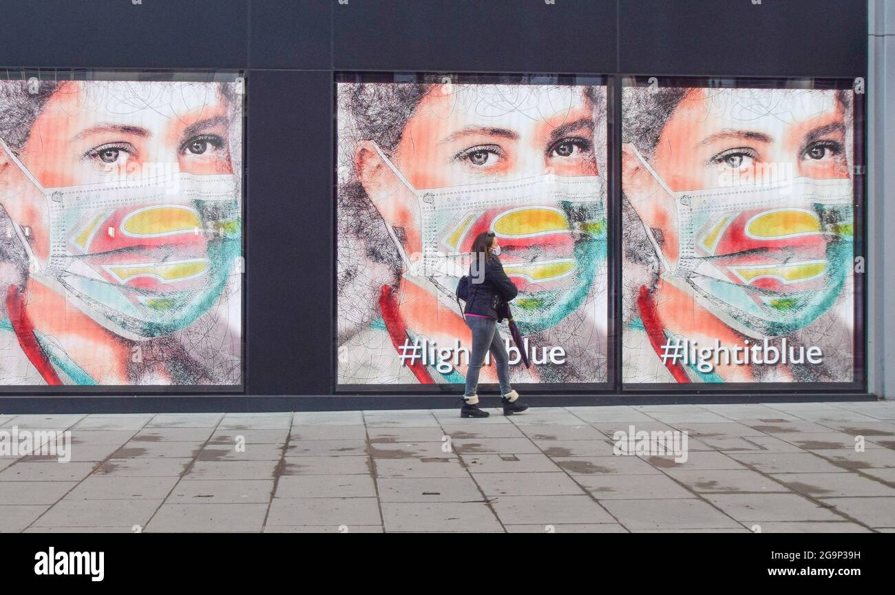 A woman walks past the screens displaying a medical worker with a ...
