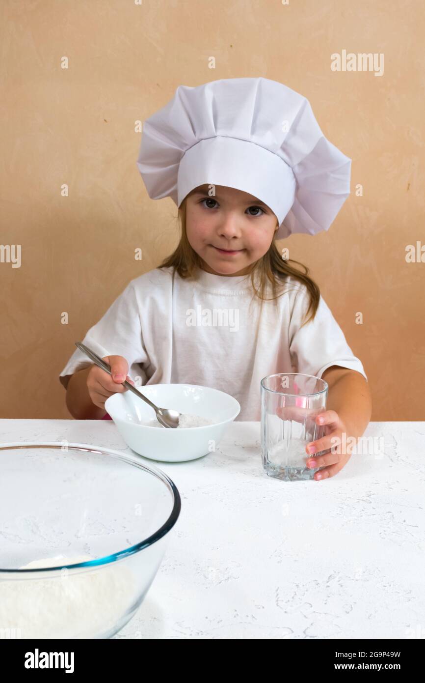 A little girl dressed as a cook kneads the dough. Cooking child ...