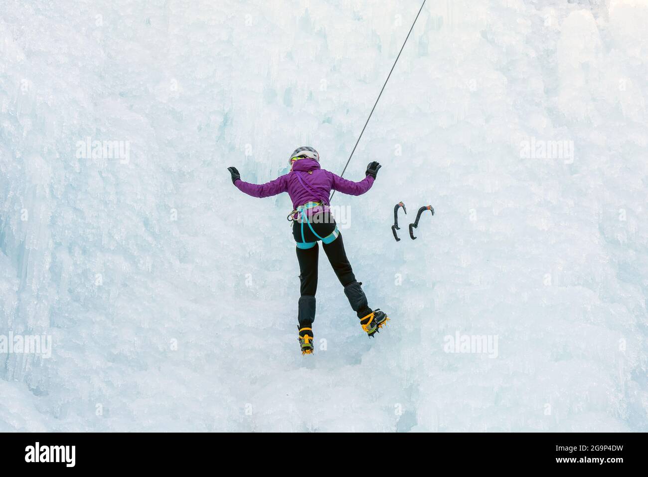 Female ice climber descending down an ice waterfall, stepping backward ...