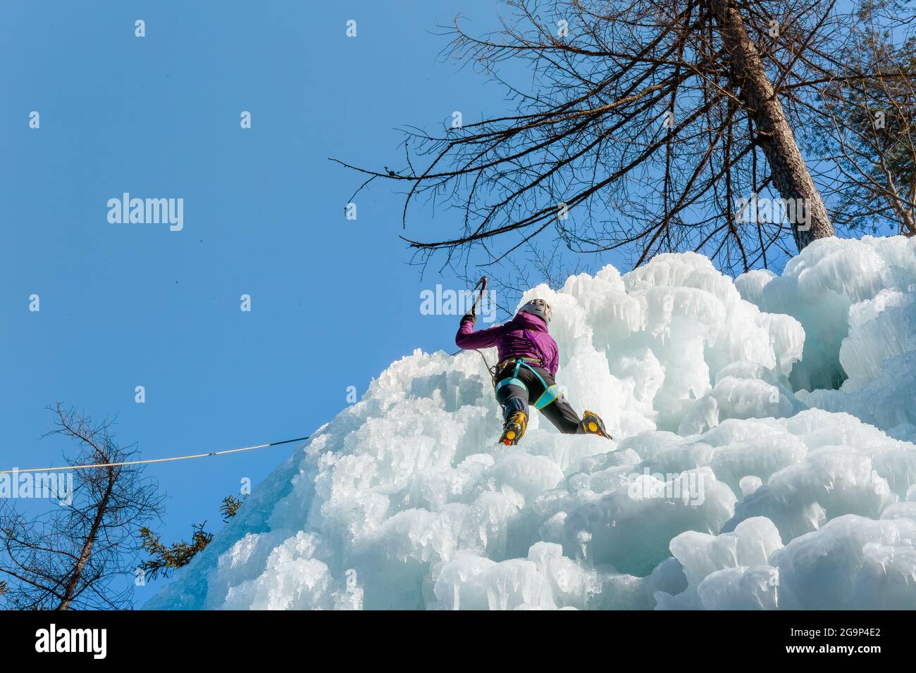 Female ice climber climbing up the side of an icy slope with bumps ...