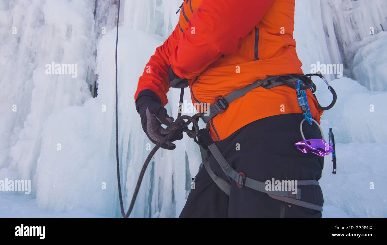 Close up shot of Caucasian male ice climber tying a rope to his harness ...