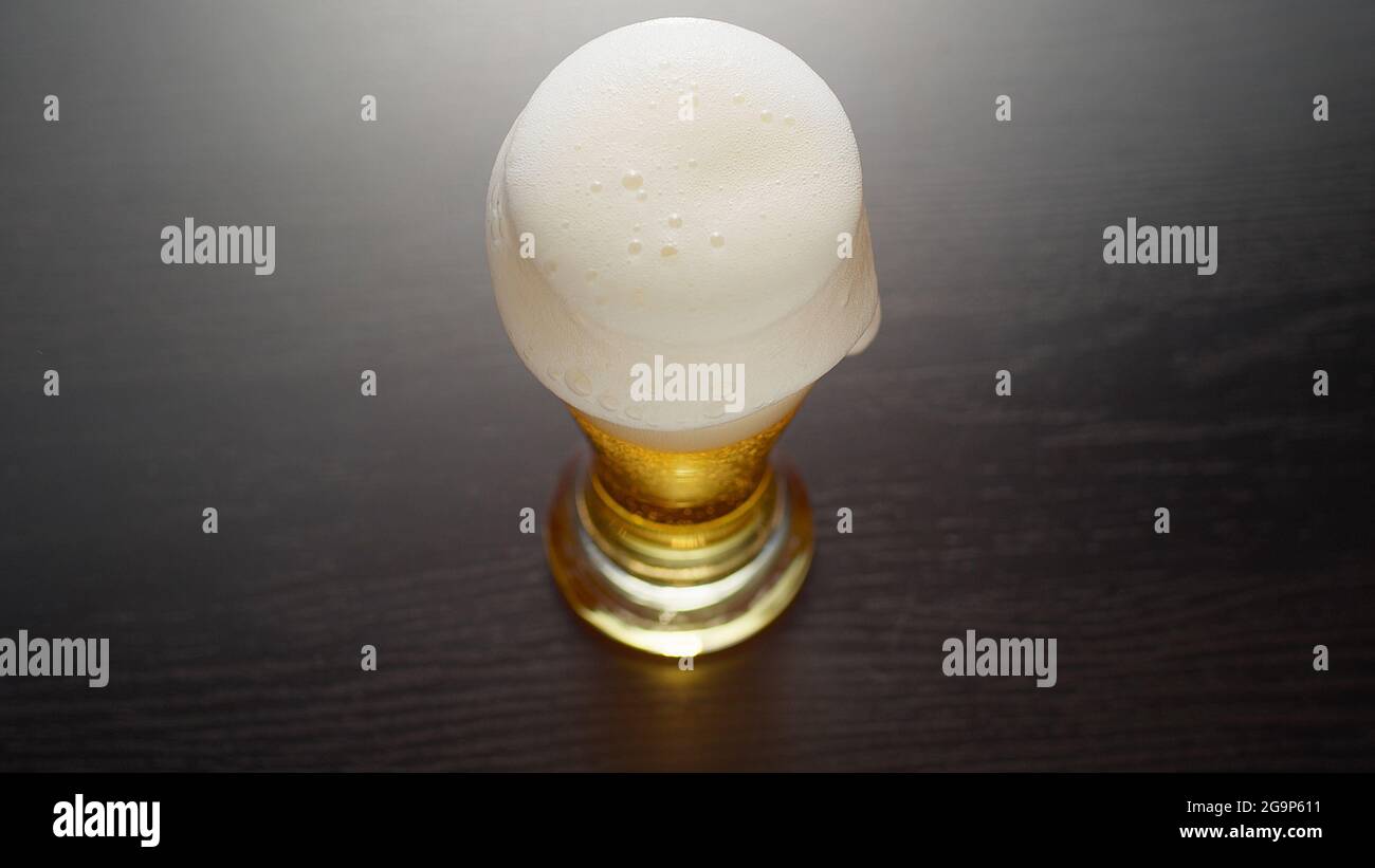 Beer in glass overflowed. Half pint of frothy fresh lager beer on table ...