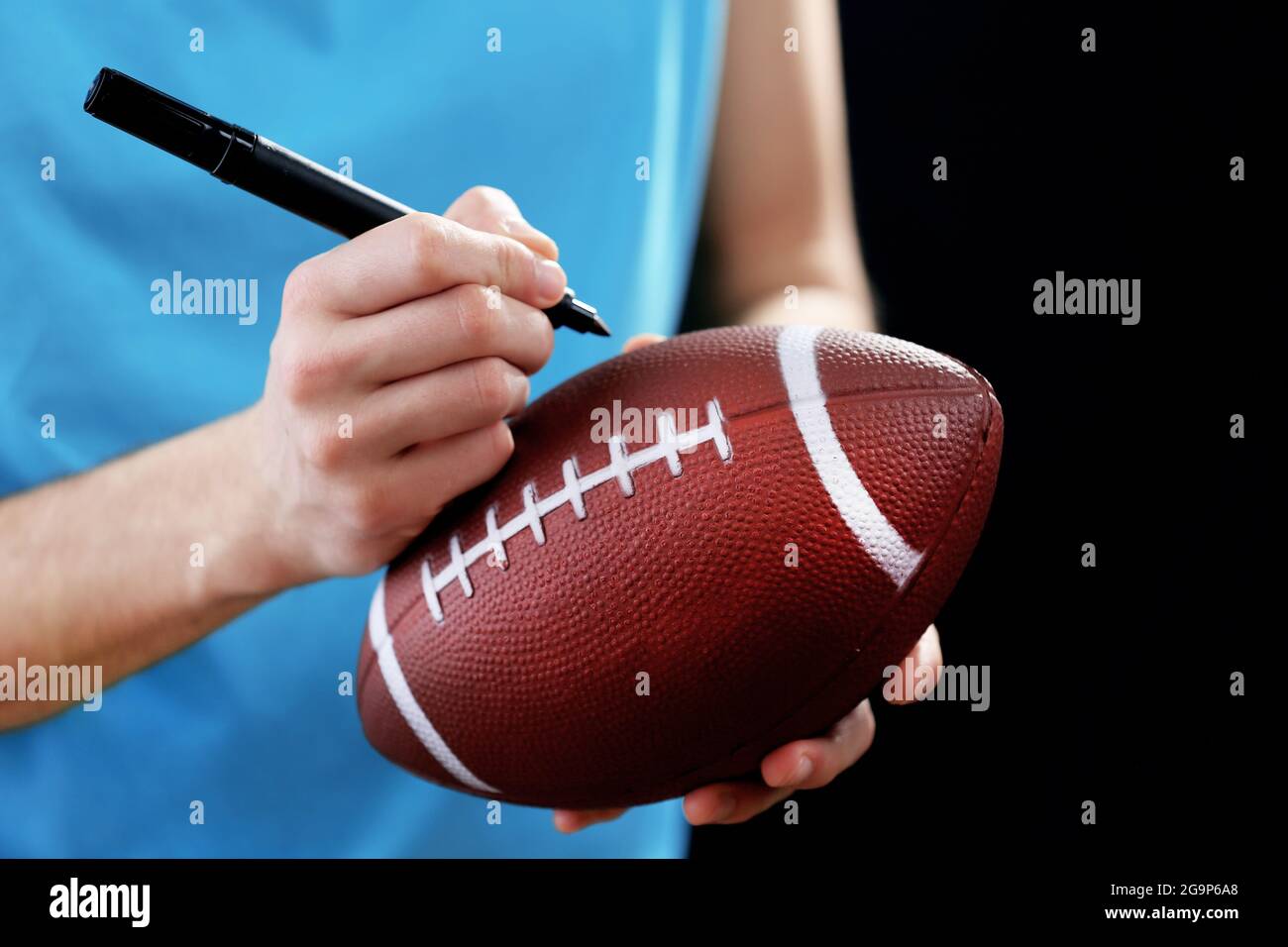 American football star signing autograph on ball on black background ...