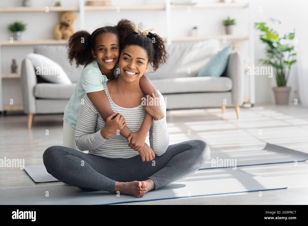 Sporty black mother and daughter sitting on fitness mat, embracing ...