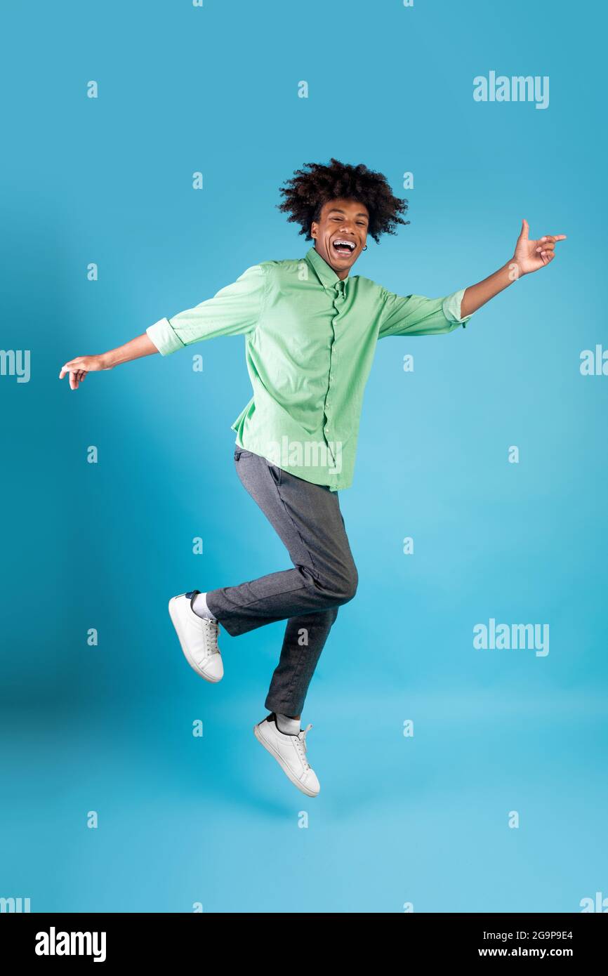 Joyful black guy jumping up in the air and showing funny figures ...