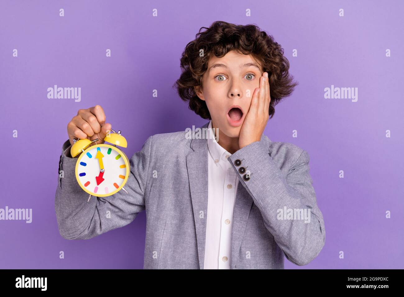 Photo of amazed speechless small guy hold alarm clock palm cheek wear ...