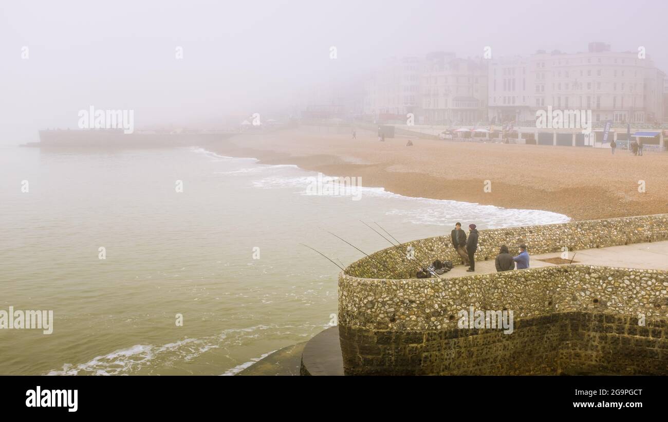 Four people fishing from a jetty next to Brighton Pier in Brighton ...