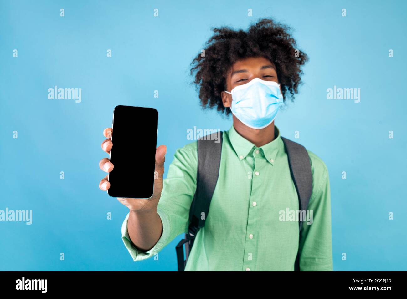 Black student guy in protective mask holding smartphone with blank ...