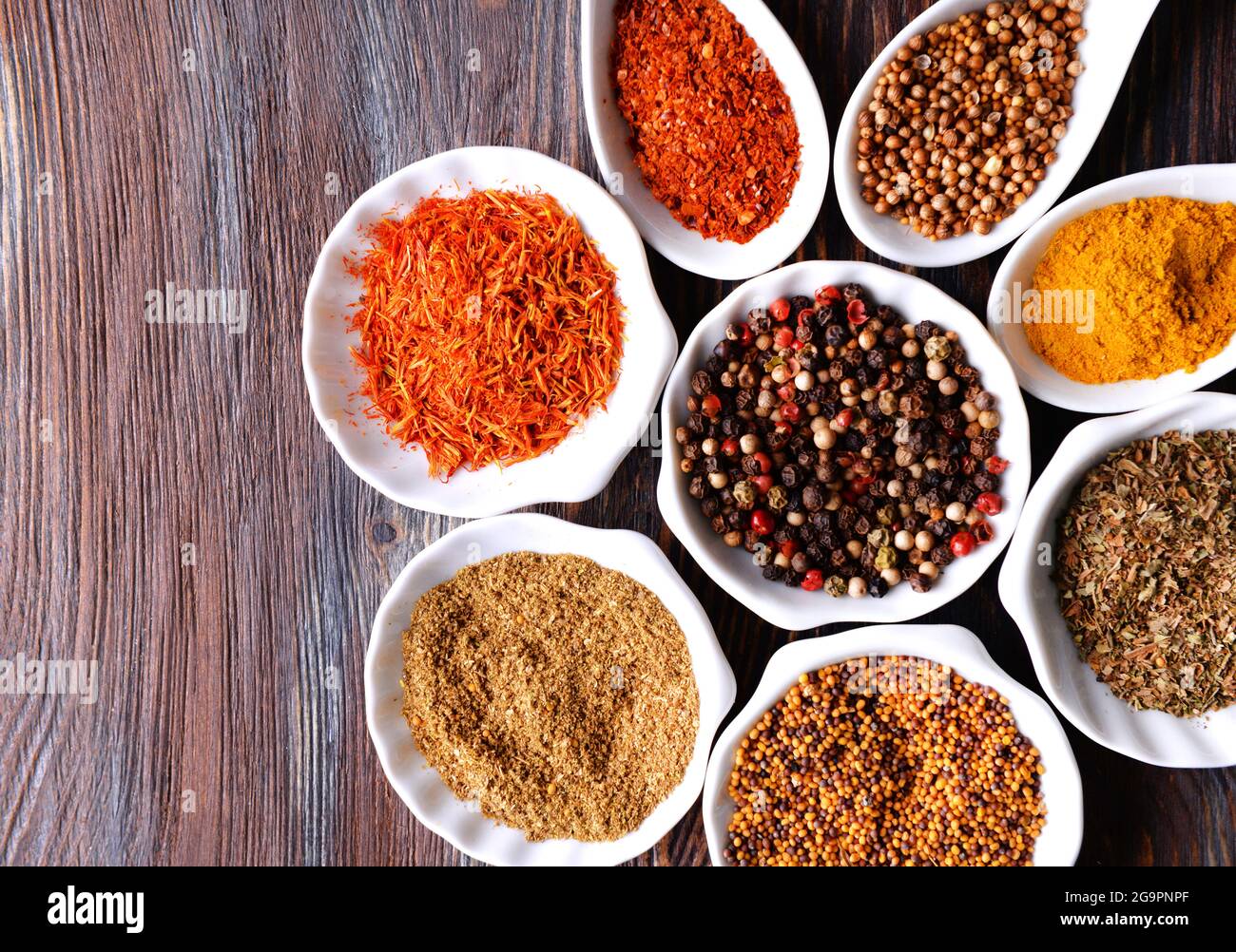 Different kinds of spices in ceramics bowls and spoons on wooden ...