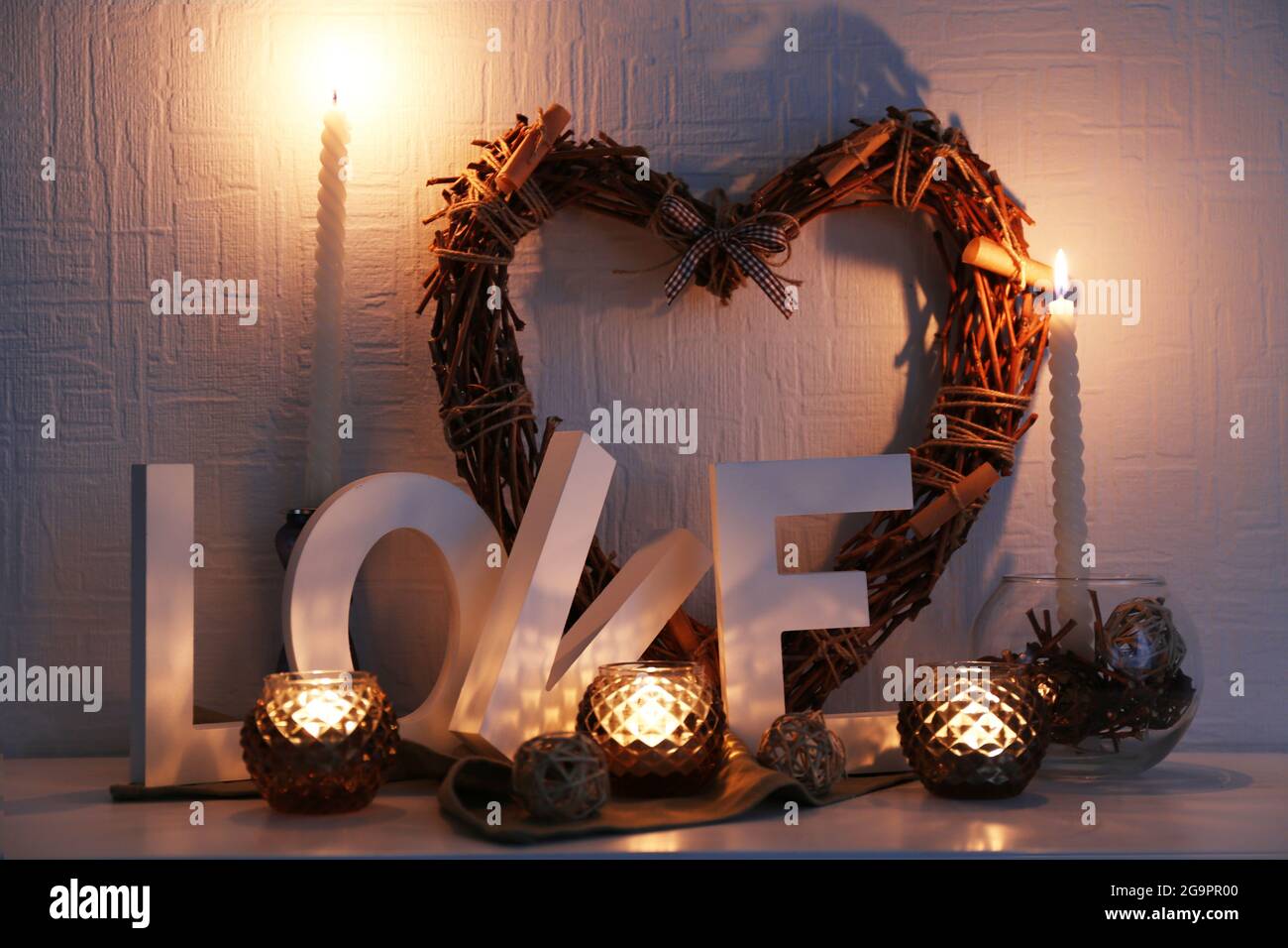 Romantic still life with wicker heart and candle lights on mantelpiece ...