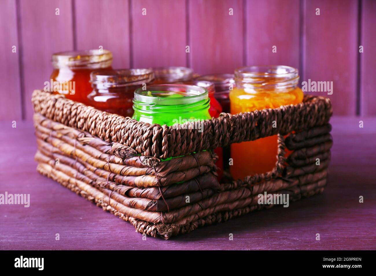 Homemade jars of fruits jam in wicker basket and color wooden ...