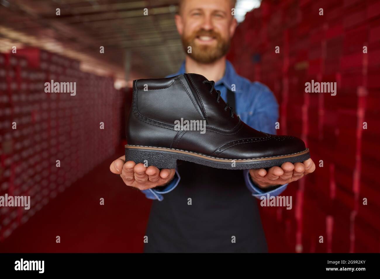 Happy warehouse worker or owner of a shoe factory showing a new black ...