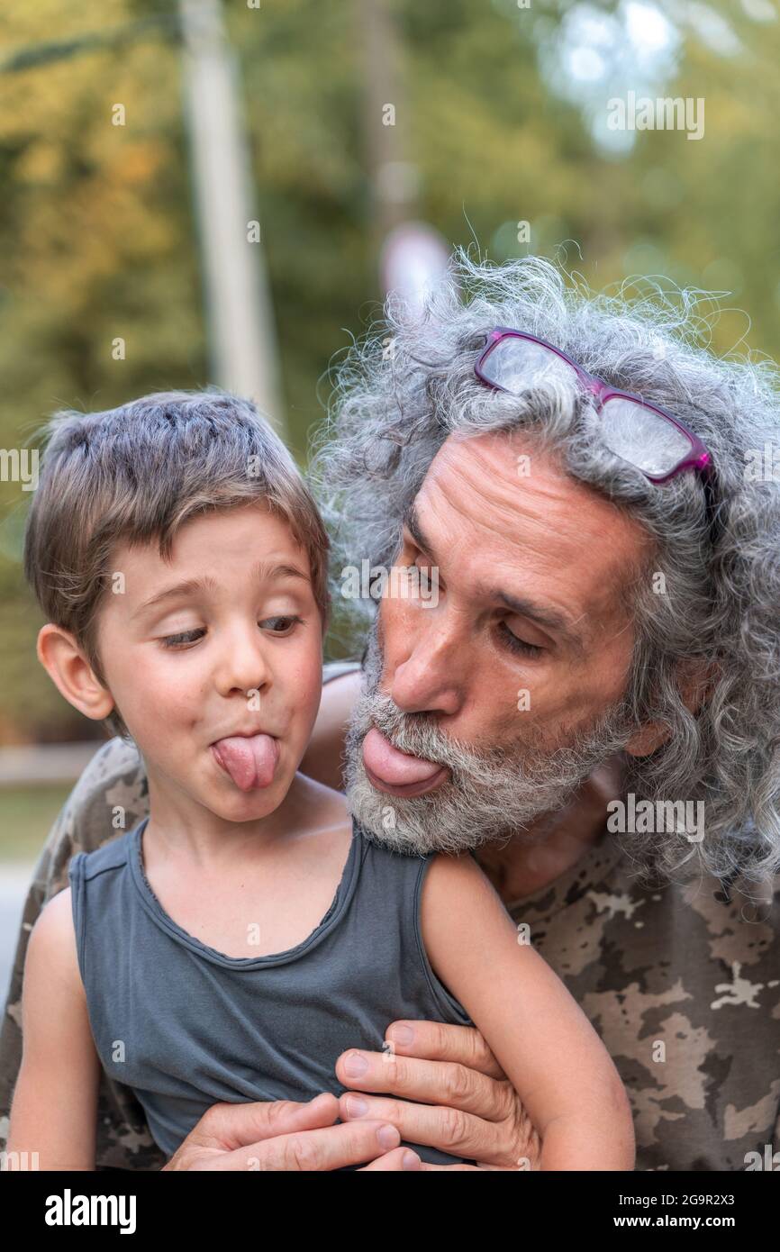 portrait of father with long gray hair and son are showing the tongue ...