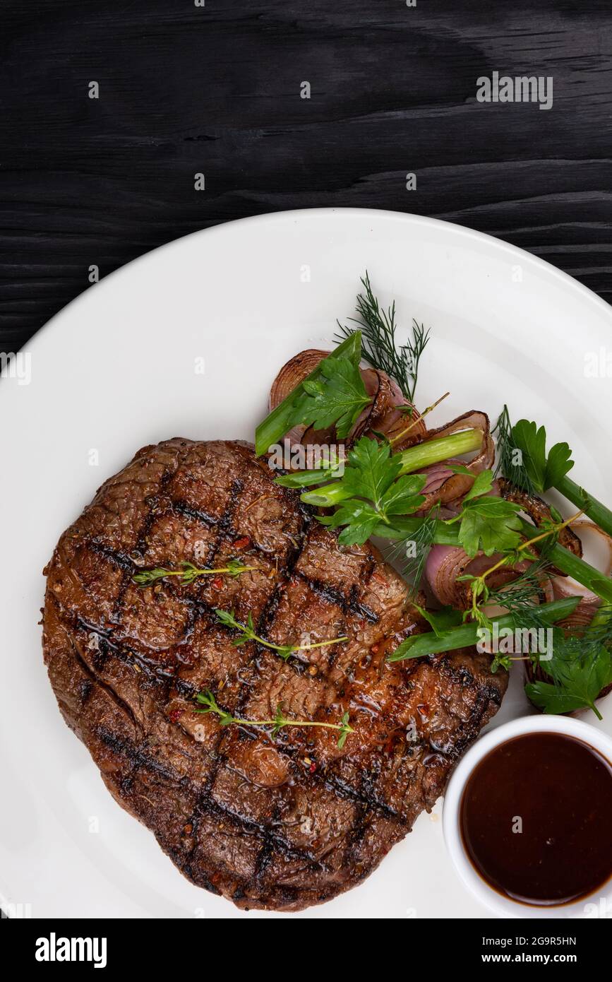 Grilled black angus steak ribeye on white plate on black wooden ...