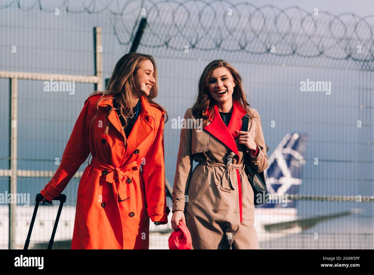 Two happy girls walking near airport, with luggage. Air travel, summer ...
