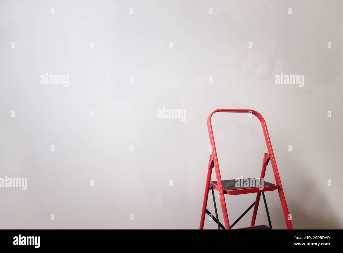 Red construction step ladder near gray wall background with copy space ...