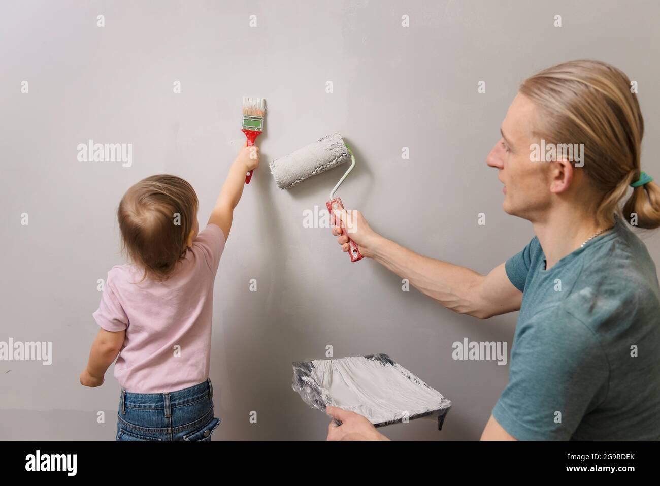 Person holding paint roller over gray wall. Father with child doing ...
