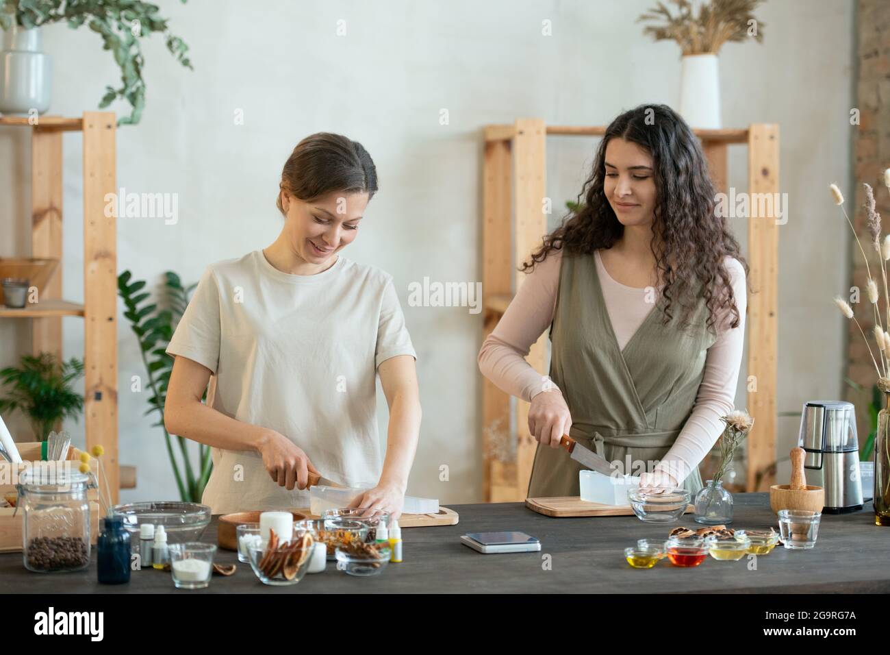 Young female pouring liquid green colorant into bowl with melted soap ...