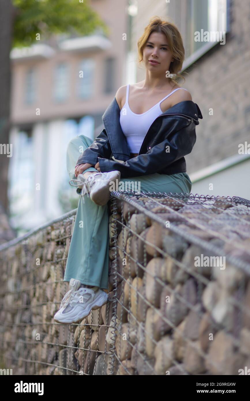 Portrait of a young pretty woman in blue shorts sitting on a bench in ...