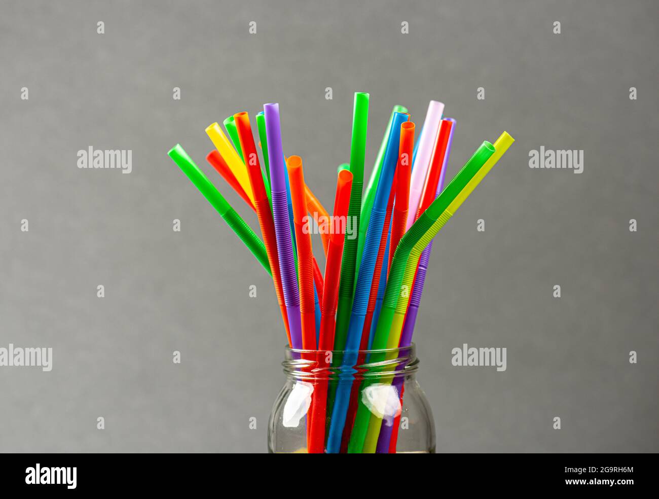Multi colored plastic straws in a jar in front of a grey background ...
