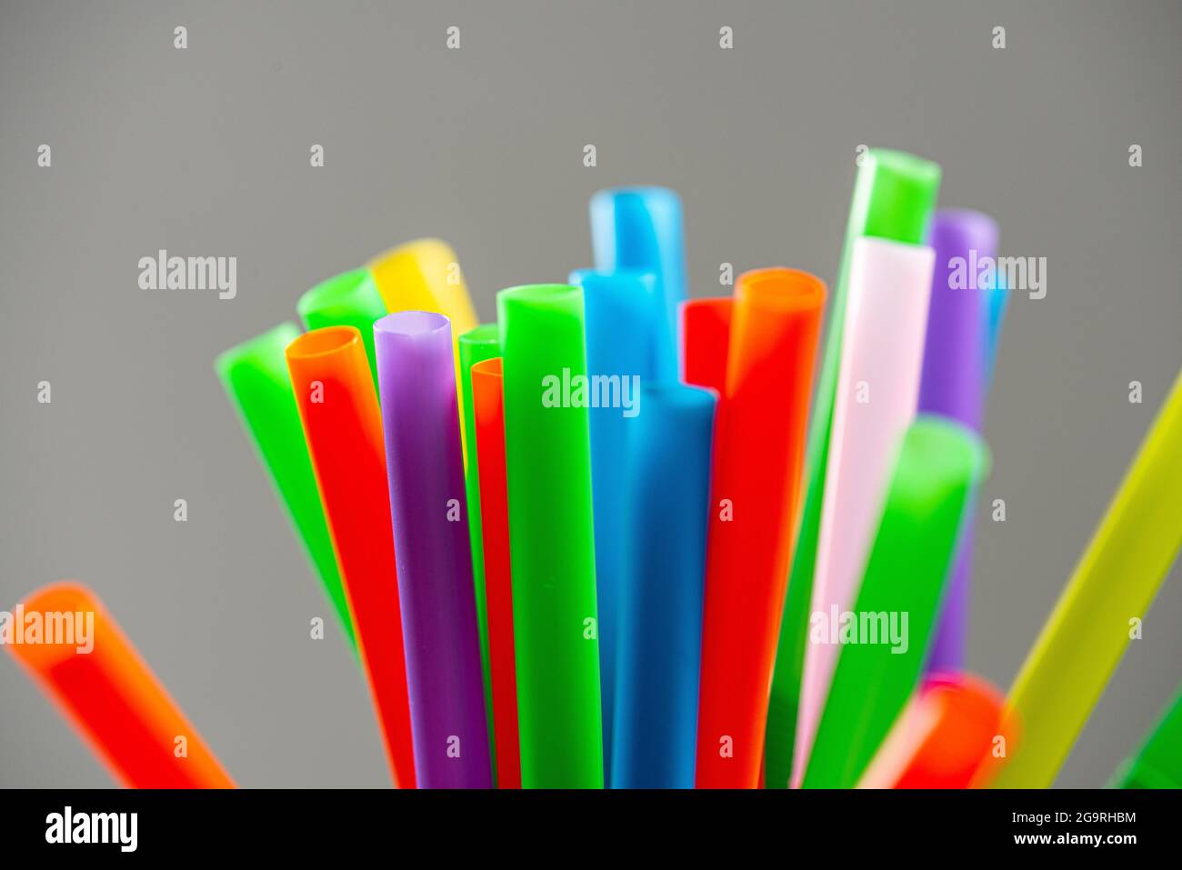 Multi colored plastic straws in a jar in front of a grey background ...