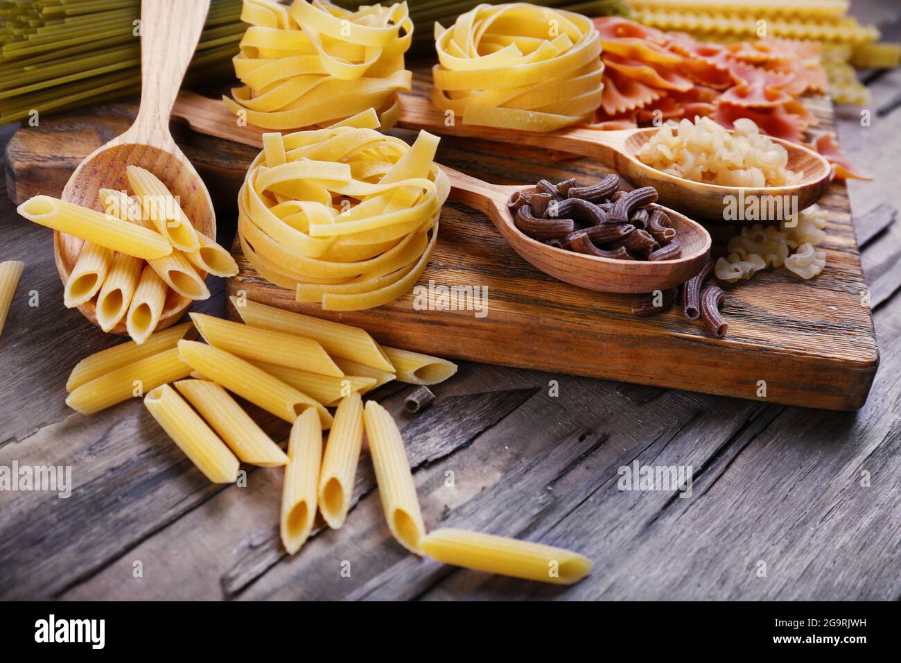 Different types of pasta on cutting board and wooden table background ...