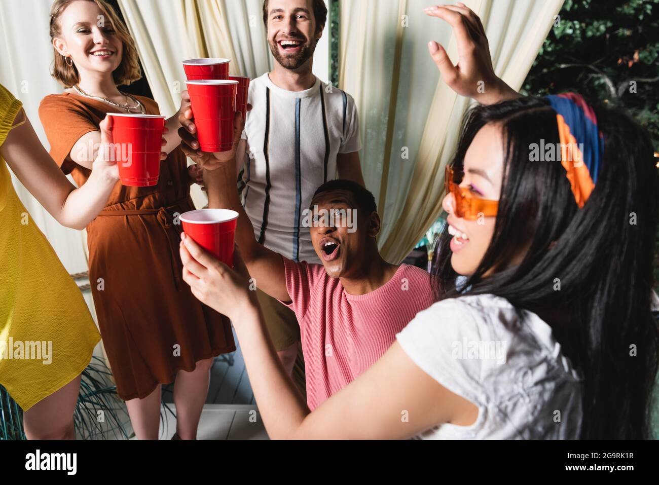 Excited african american friend holding plastic cup near friends in ...
