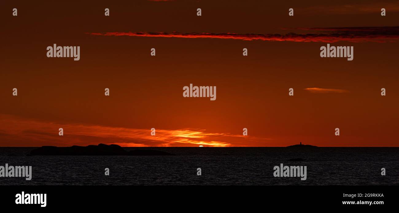 The sun setting in the ocean with small islands and a lighthouse in the ...