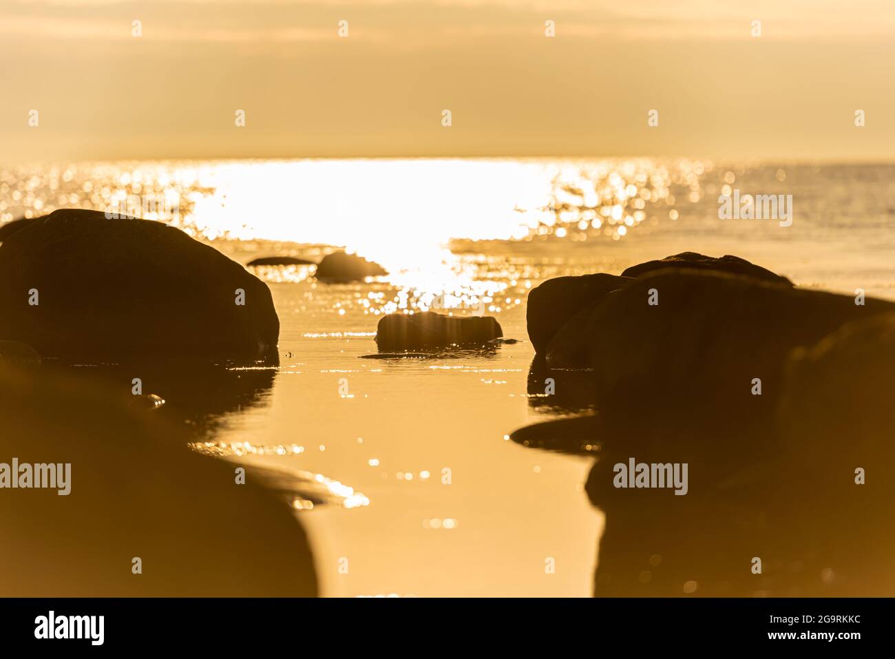 Sunset over rocks by a beach Stock Photo - Alamy