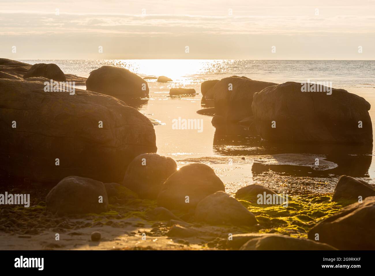 Sunset over rocks by a beach Stock Photo - Alamy