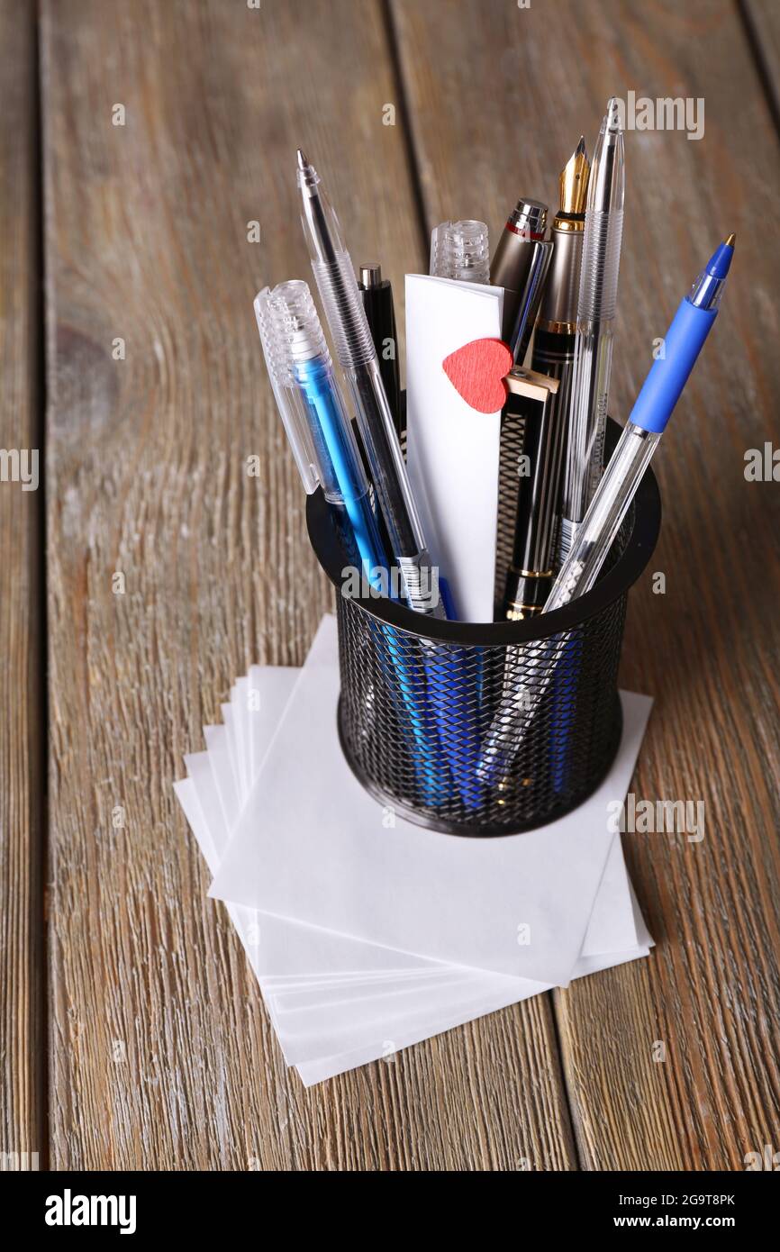 Different pens in metal holder with paper notes on wooden planks ...