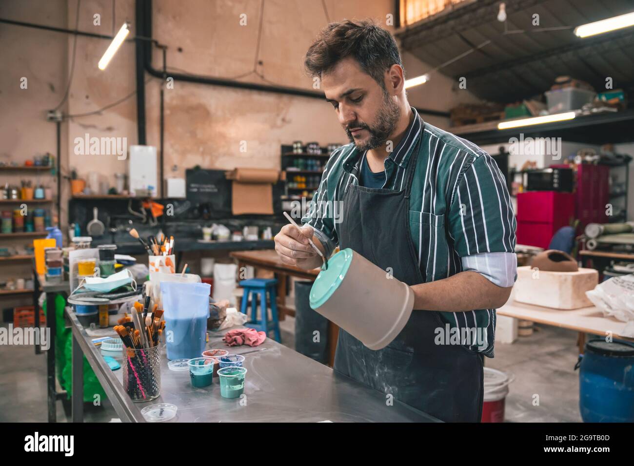 Adult Hispanic man painting a clay pot in a workshop with a blurred ...