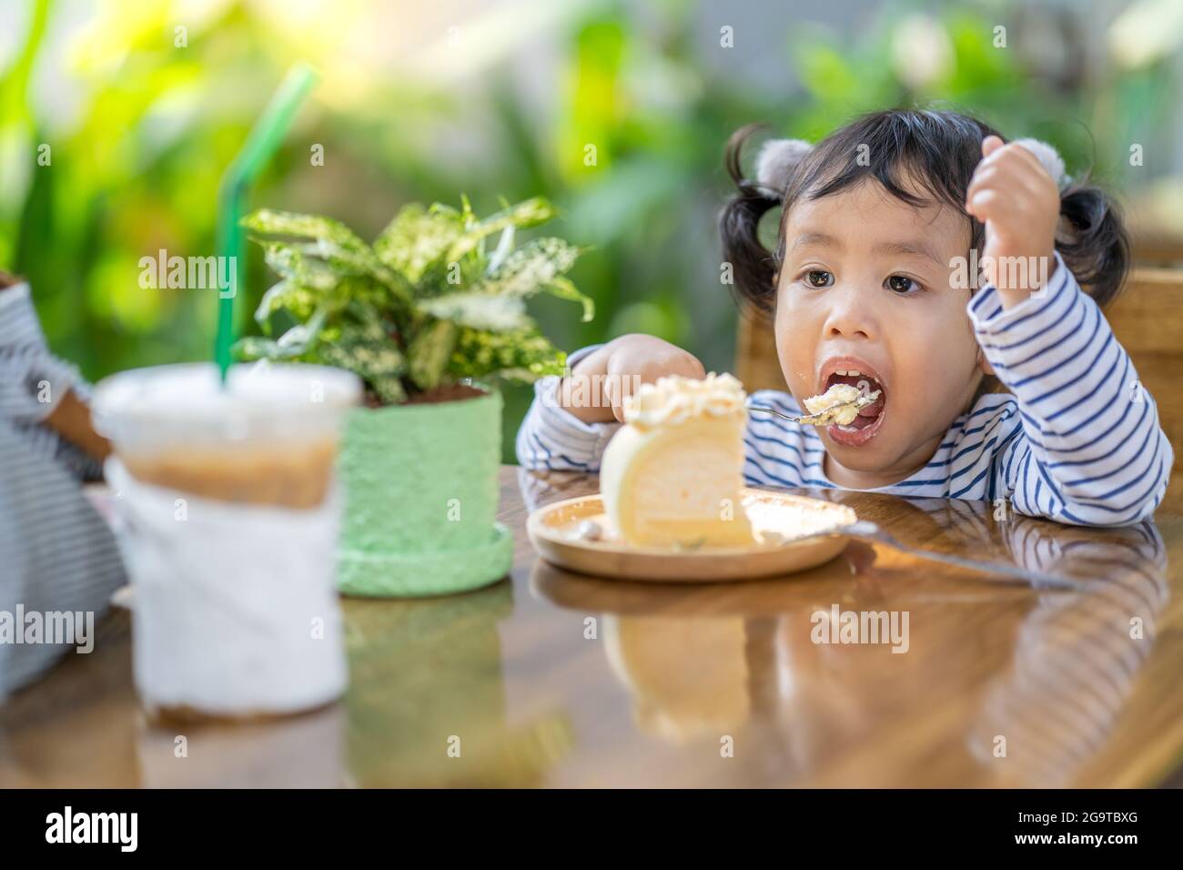 Cute Asian female child eating a piece of cake Stock Photo - Alamy