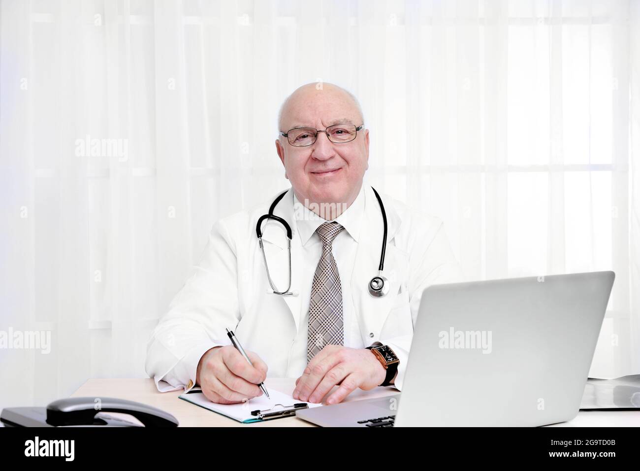 Portrait of professional doctor at table in his office on white curtain ...
