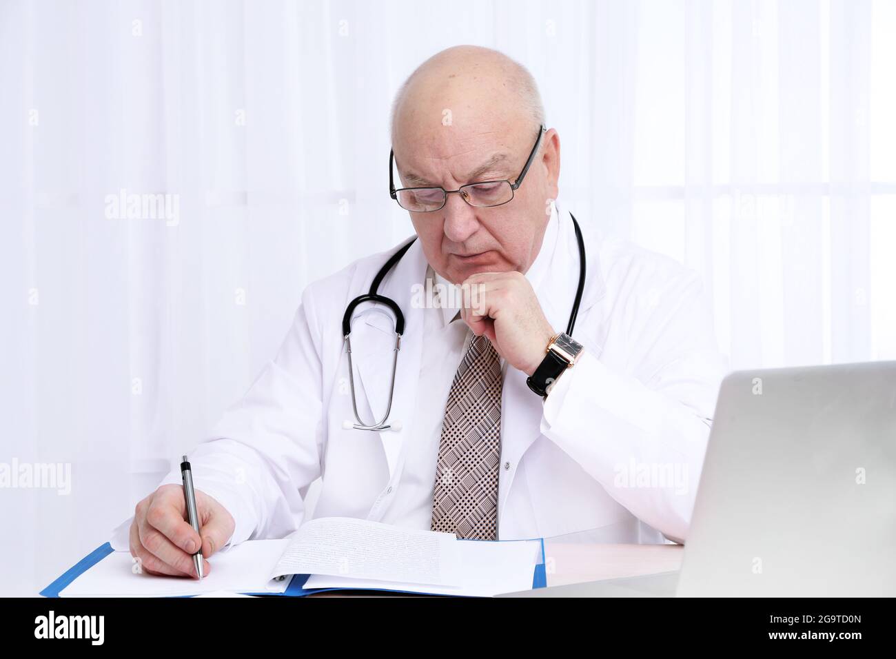 Portrait of professional doctor at table in his office on white curtain ...
