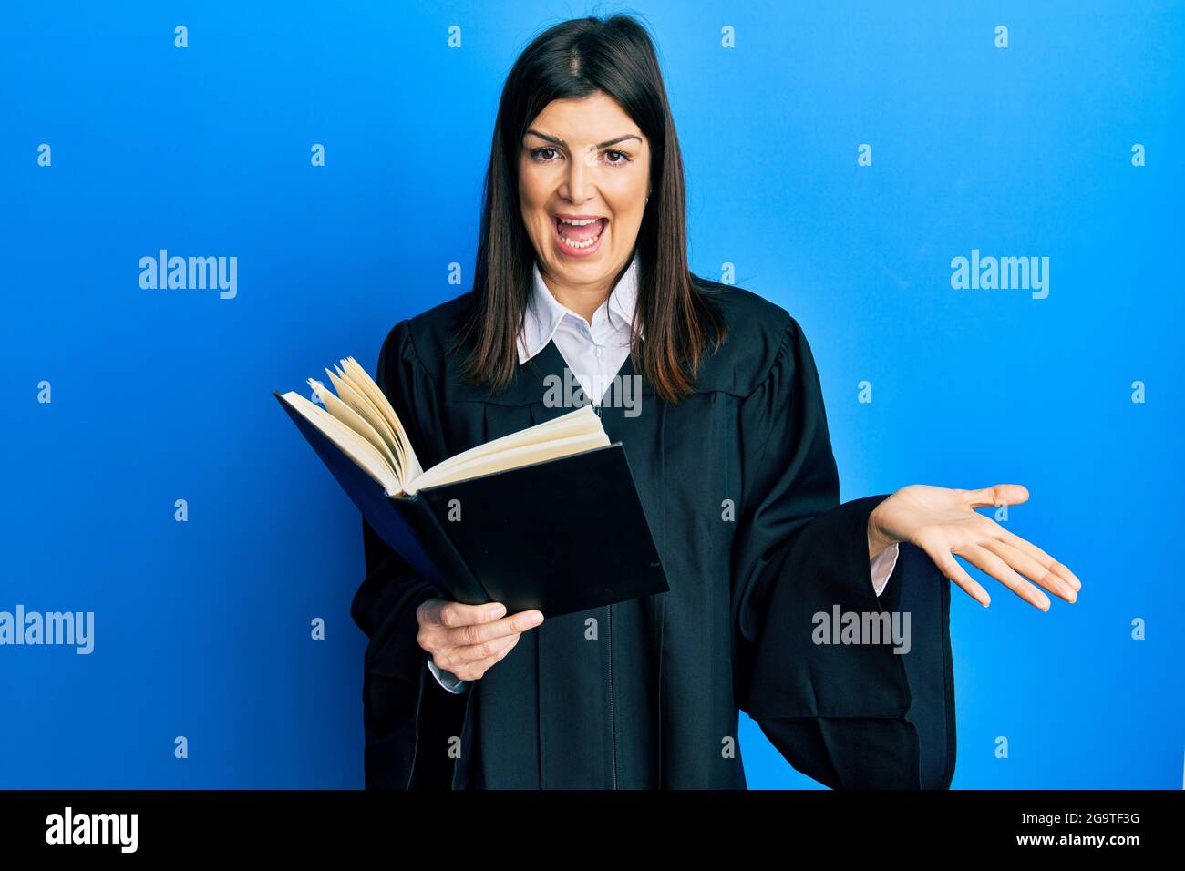 Young hispanic woman wearing judge uniform reading book celebrating ...