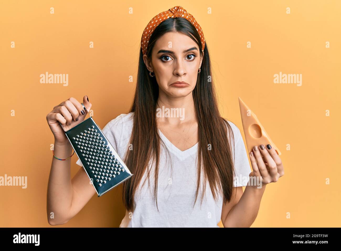 Beautiful brunette young woman holding grater and cheese depressed and ...